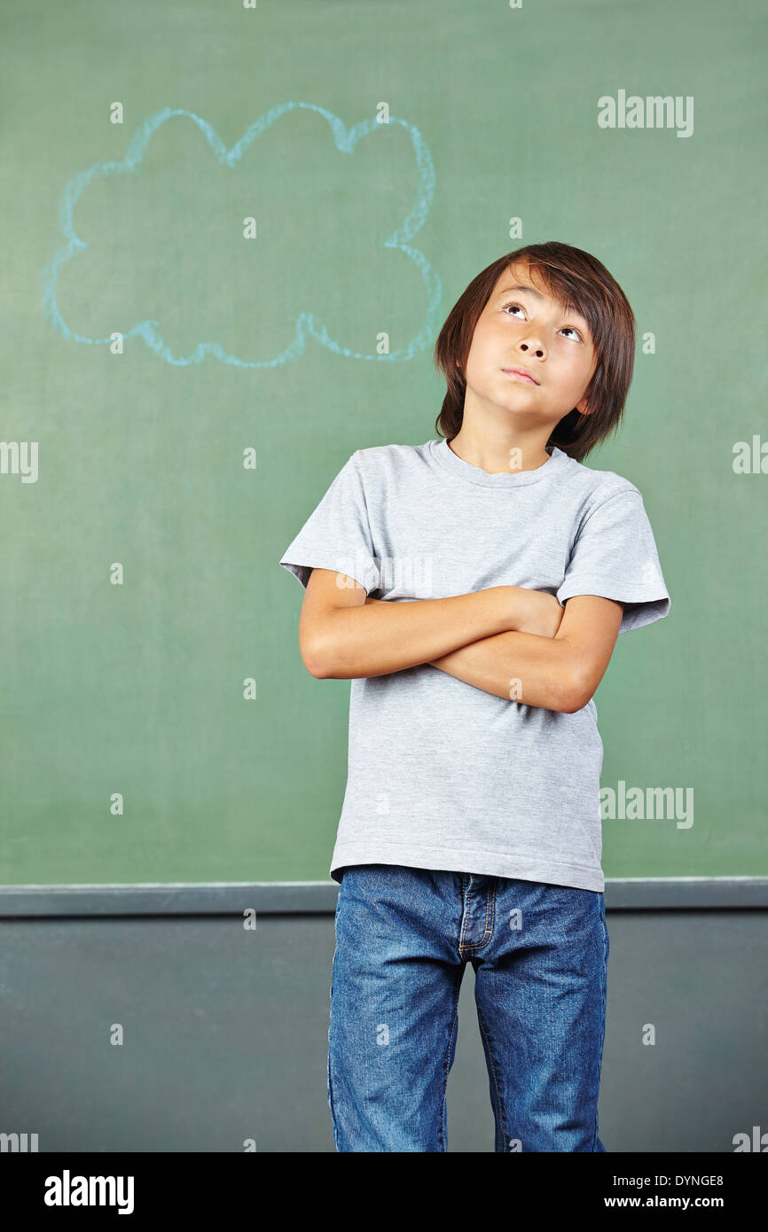 Asian child thinking in elementary school in front of chalkboard with ...