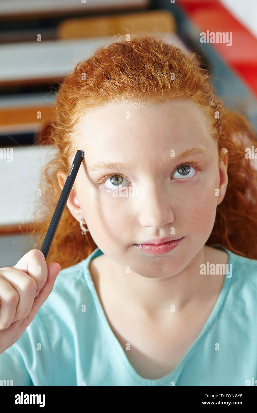 Girl in class thinking with pencil on her forehead in elementary school ...