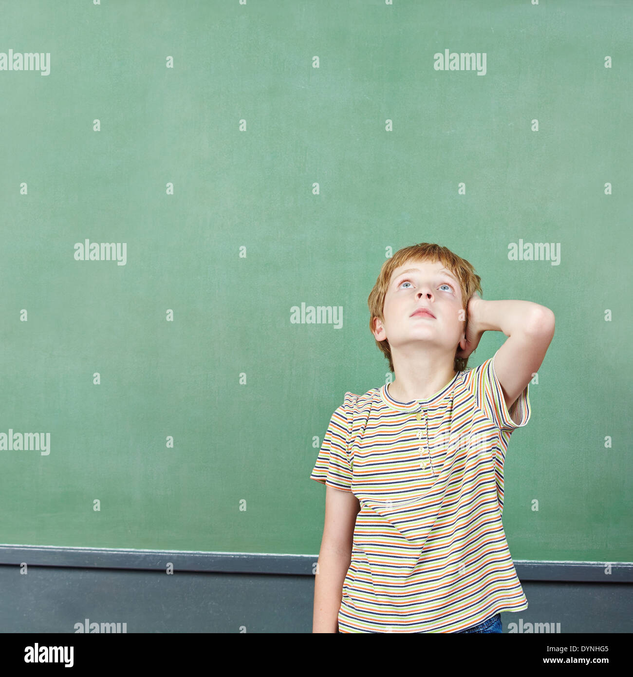 Boy standing in front of empty chalkboard thinking in elementary school ...