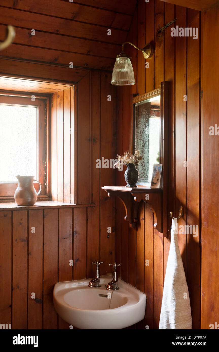 Wood panelled room corner with small wash basin and wooden mirror with ...