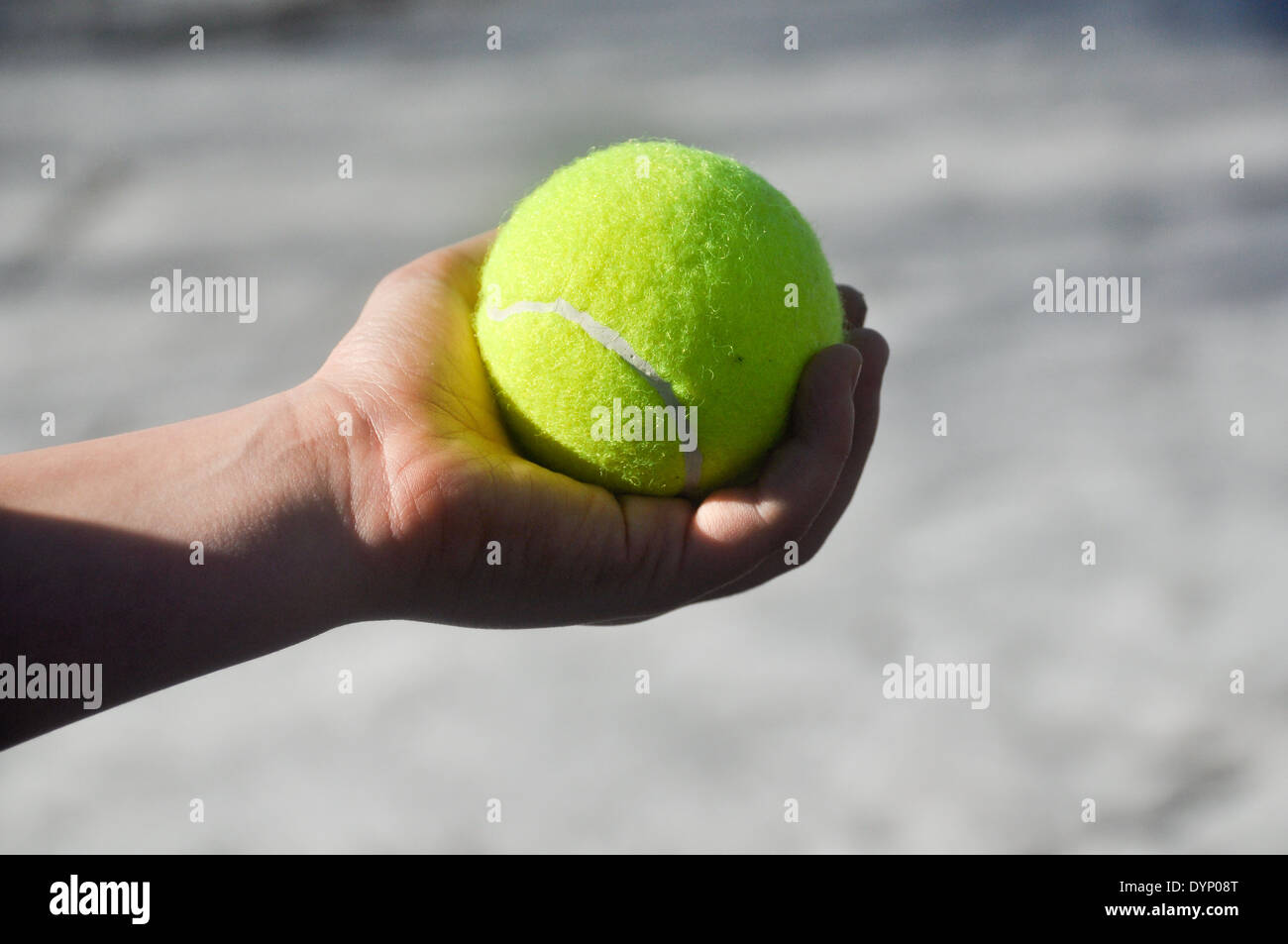Yellow tennis ball, illuminated by the sun, lies in a child's hands ...