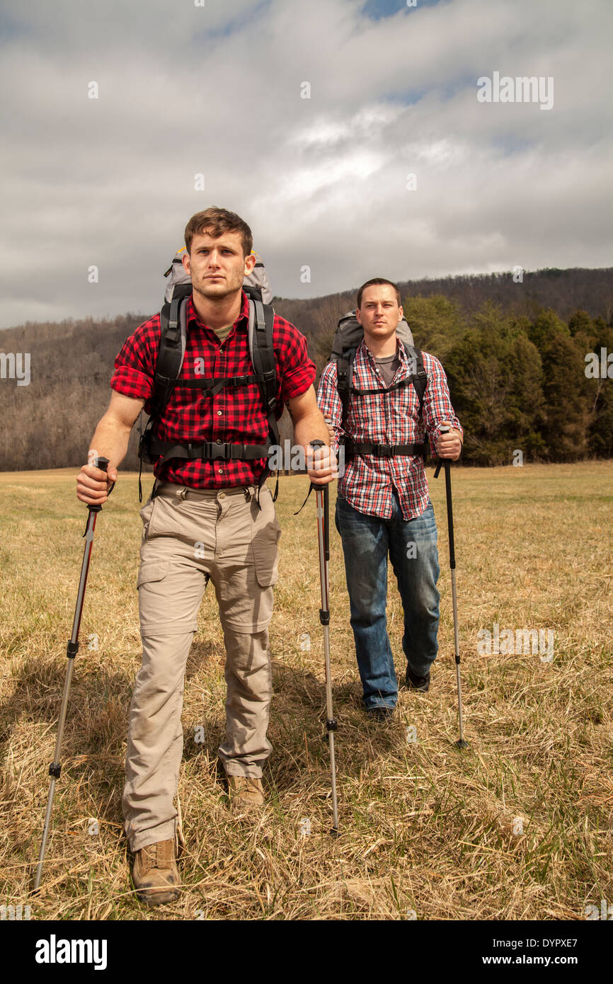 two hikers with backpacks and walking sticks walking to the campsite ...