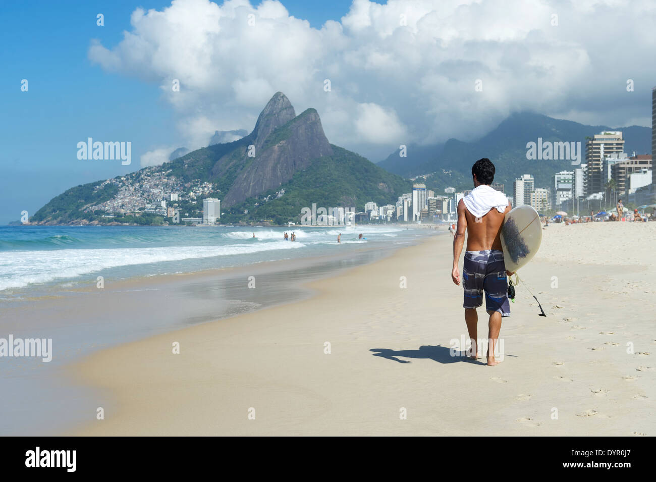 Brazilian surfer walking with surfboard toward Two Brothers Mountain on ...