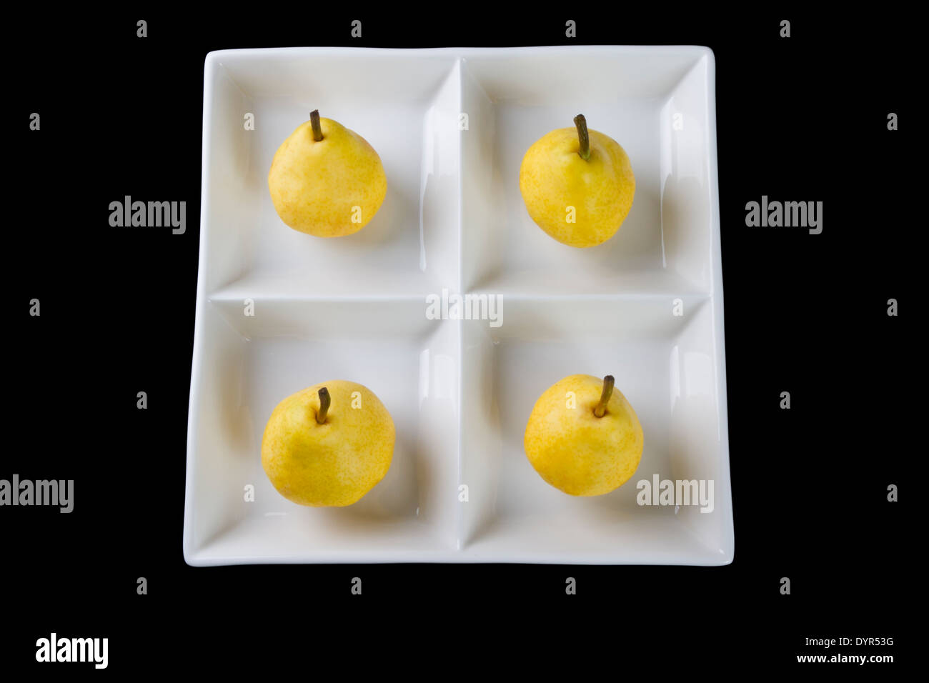 Four pears on a sectioned white china dish against a black background ...