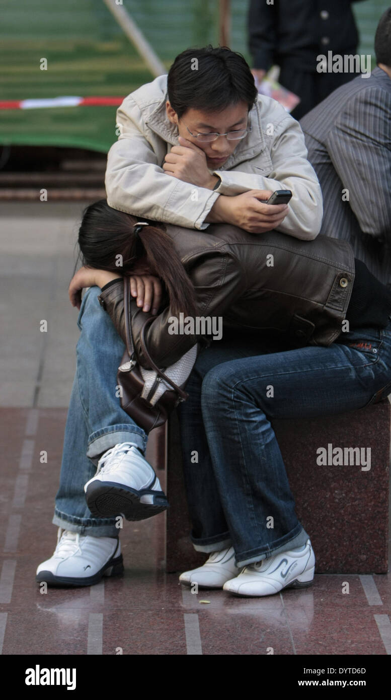 A man uses his cell phone while his girl friend have a nap on a street ...