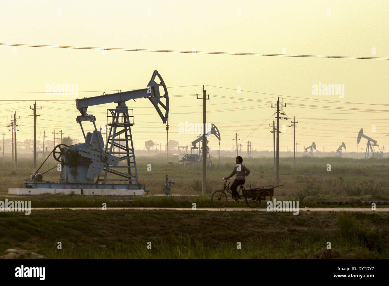 A Chinese ride on a tricycle pass by an oil well at Sinopec's Shengli ...