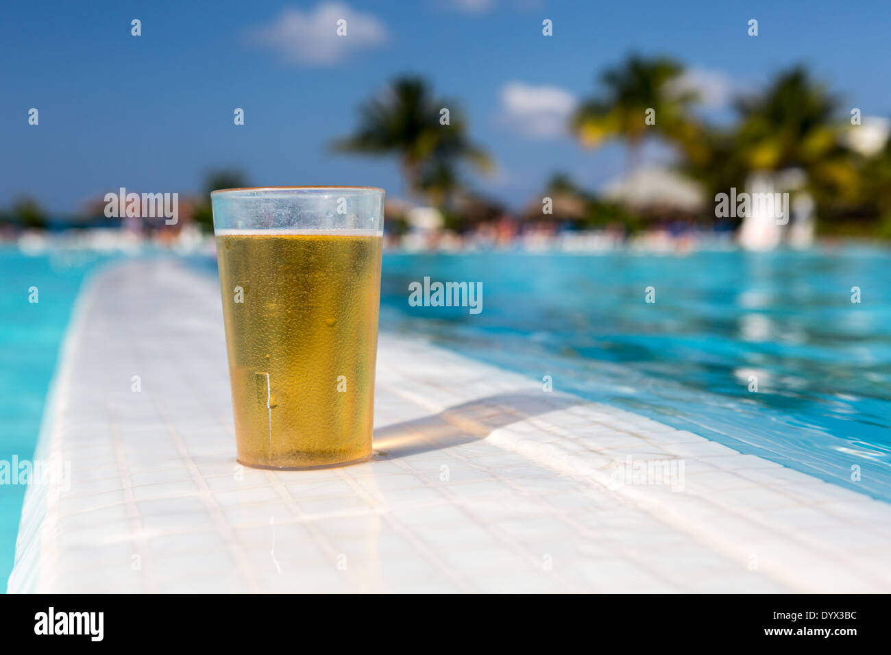 Glass of beer standing on the swimming pool ledge in an tropical resort ...