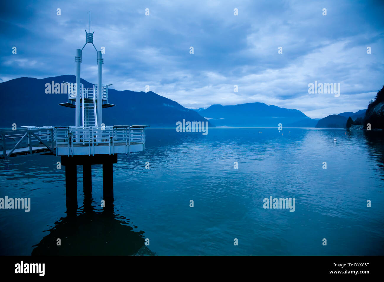 view across calm inlet water of white metal pier and gantry with ...