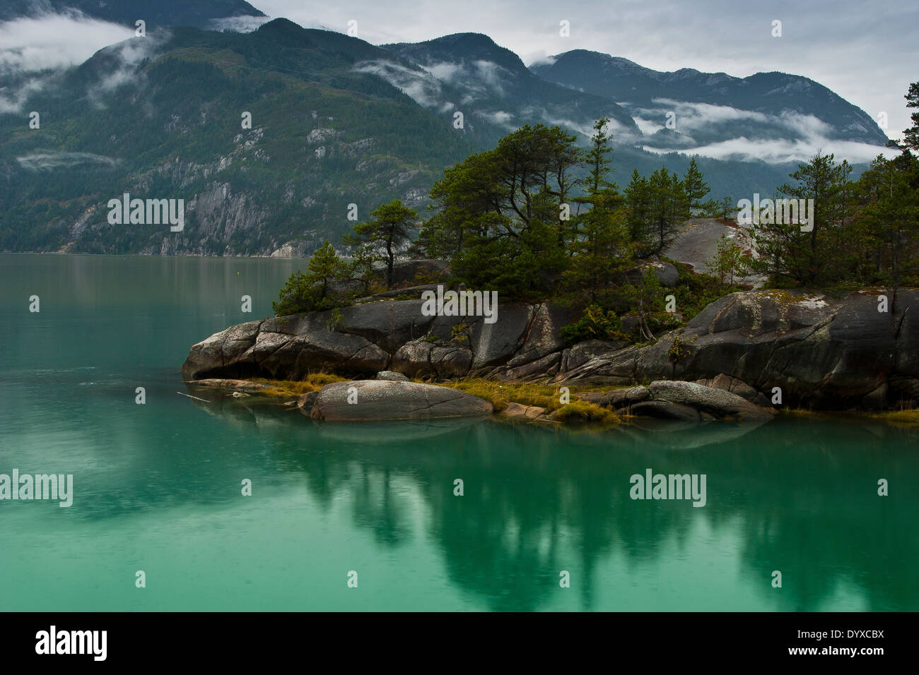 rock island with small trees in a aqua-green still & reflective inlet ...