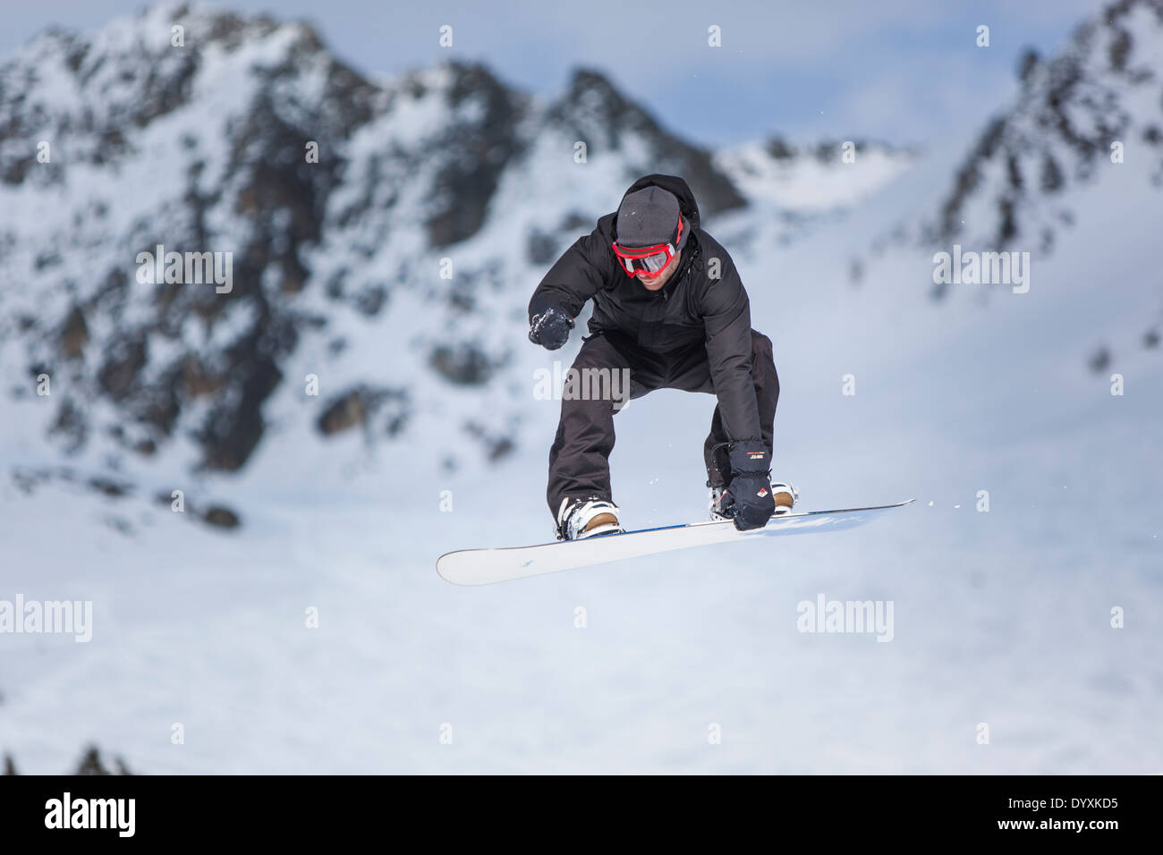 Snowboarder with woollen hat and goggles, performs a grab jump with ...
