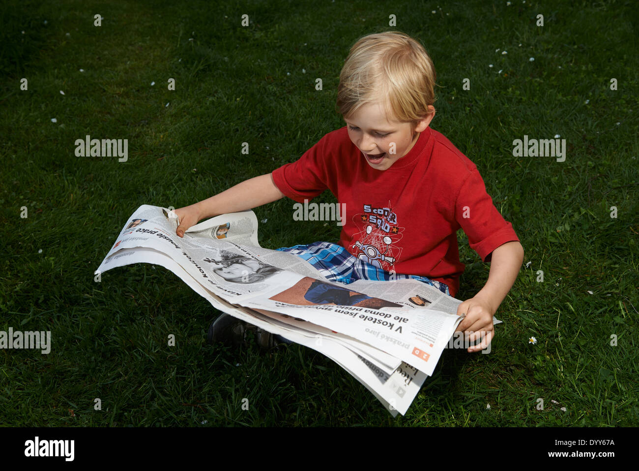 A child blond boy reading newspaper outside at green grass lawn Stock ...