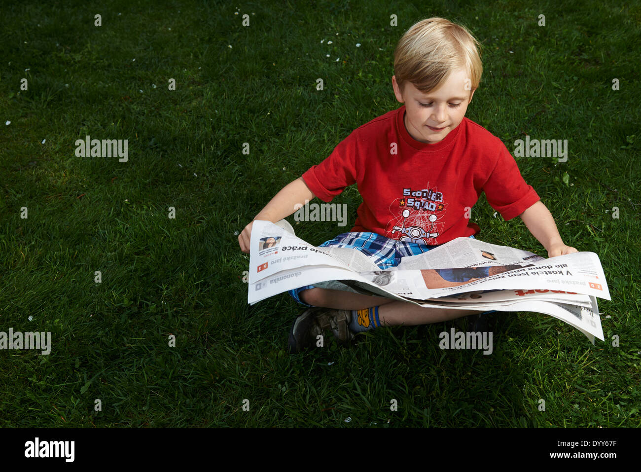 A child blond boy reading newspaper outside at green grass lawn Stock ...
