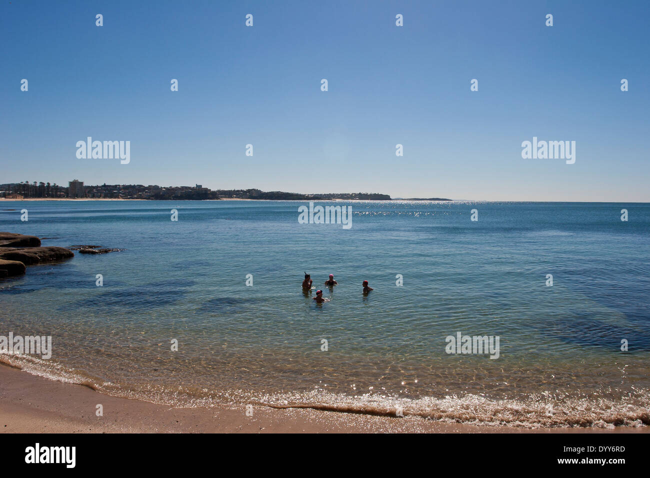 four swimmers in still aqua-blue translucent ocean water on a perfect ...