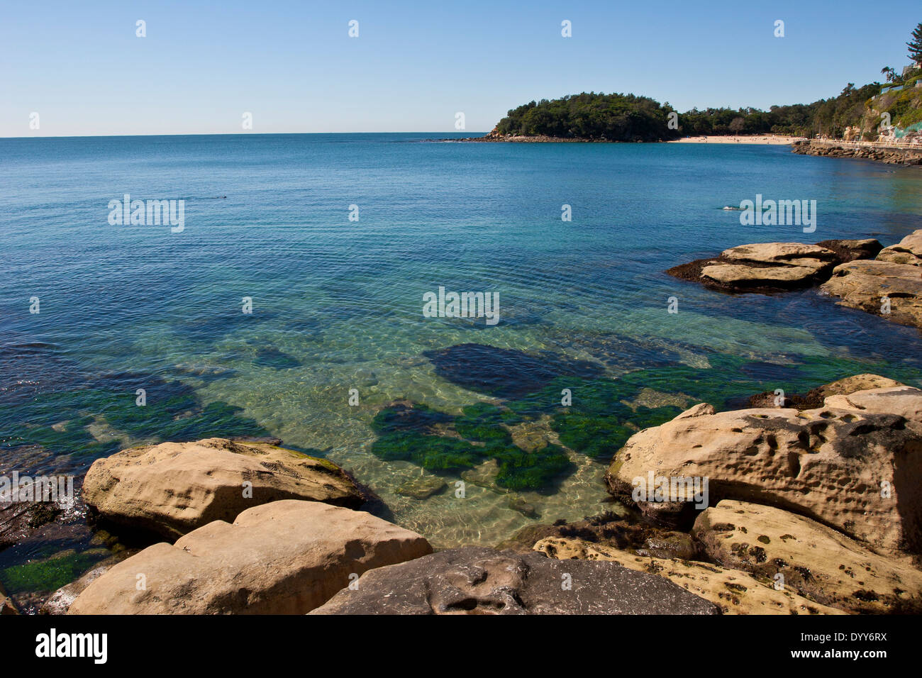 View from rocks across calm aqua-blue translucent ocean water to a ...
