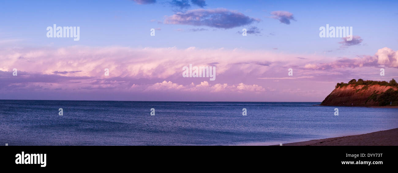 panorama of curved beach to rock headland. Sunset low lavender colour ...
