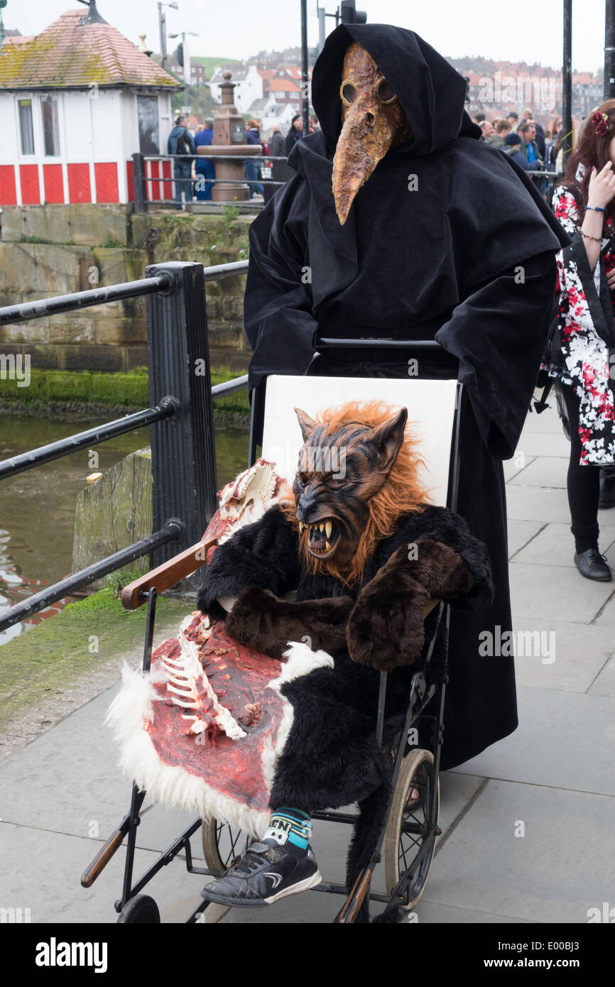 A man in a hooded cloak wearing a bird mask pushes a boy in a wolf mask ...