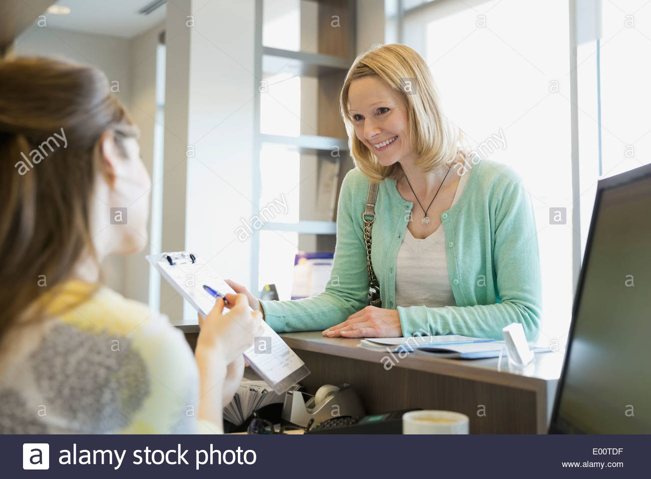 Receptionist explaining paperwork to patient in dentists office Stock ...