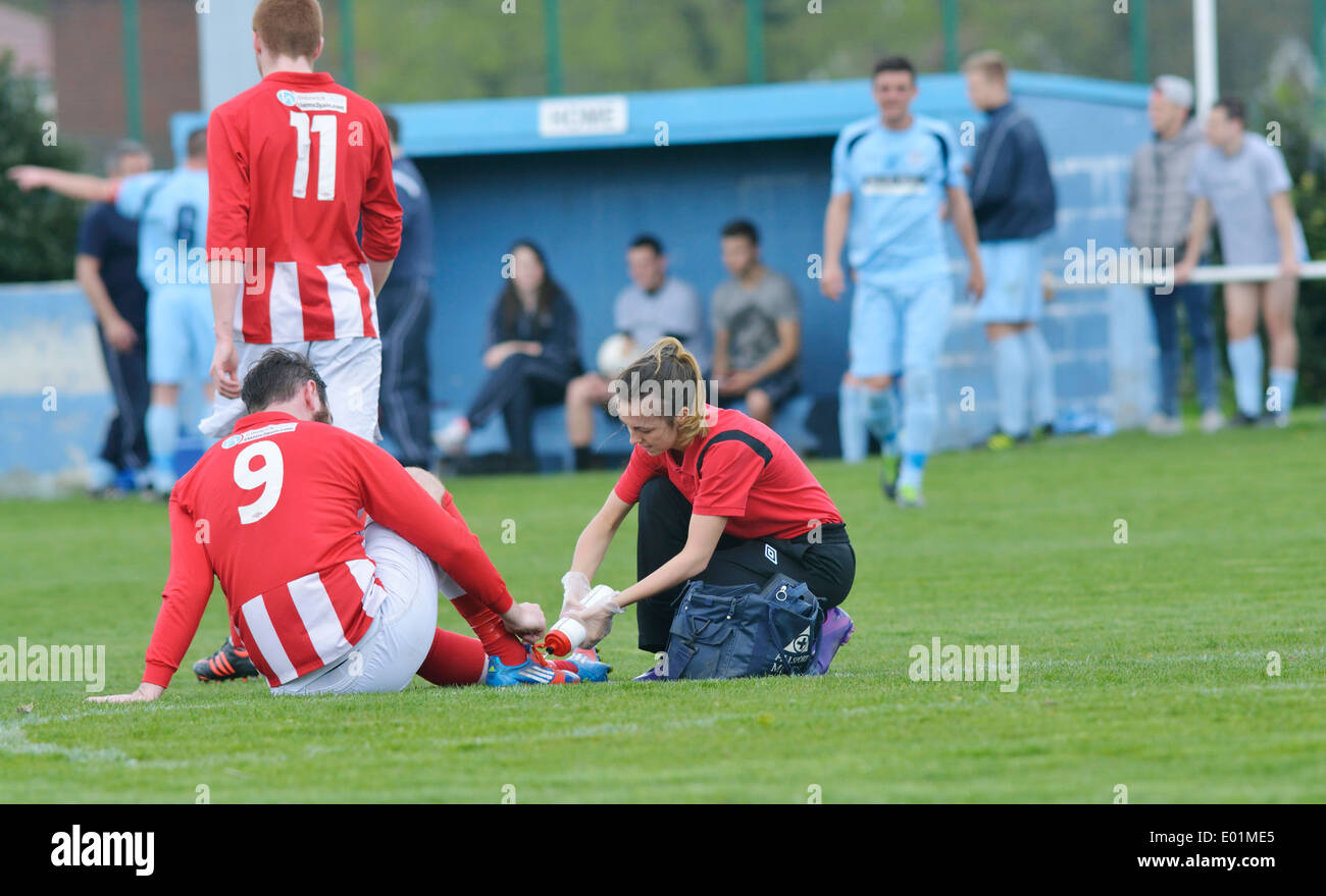 a football player sits injured on the pitch as the physiotherapists ...