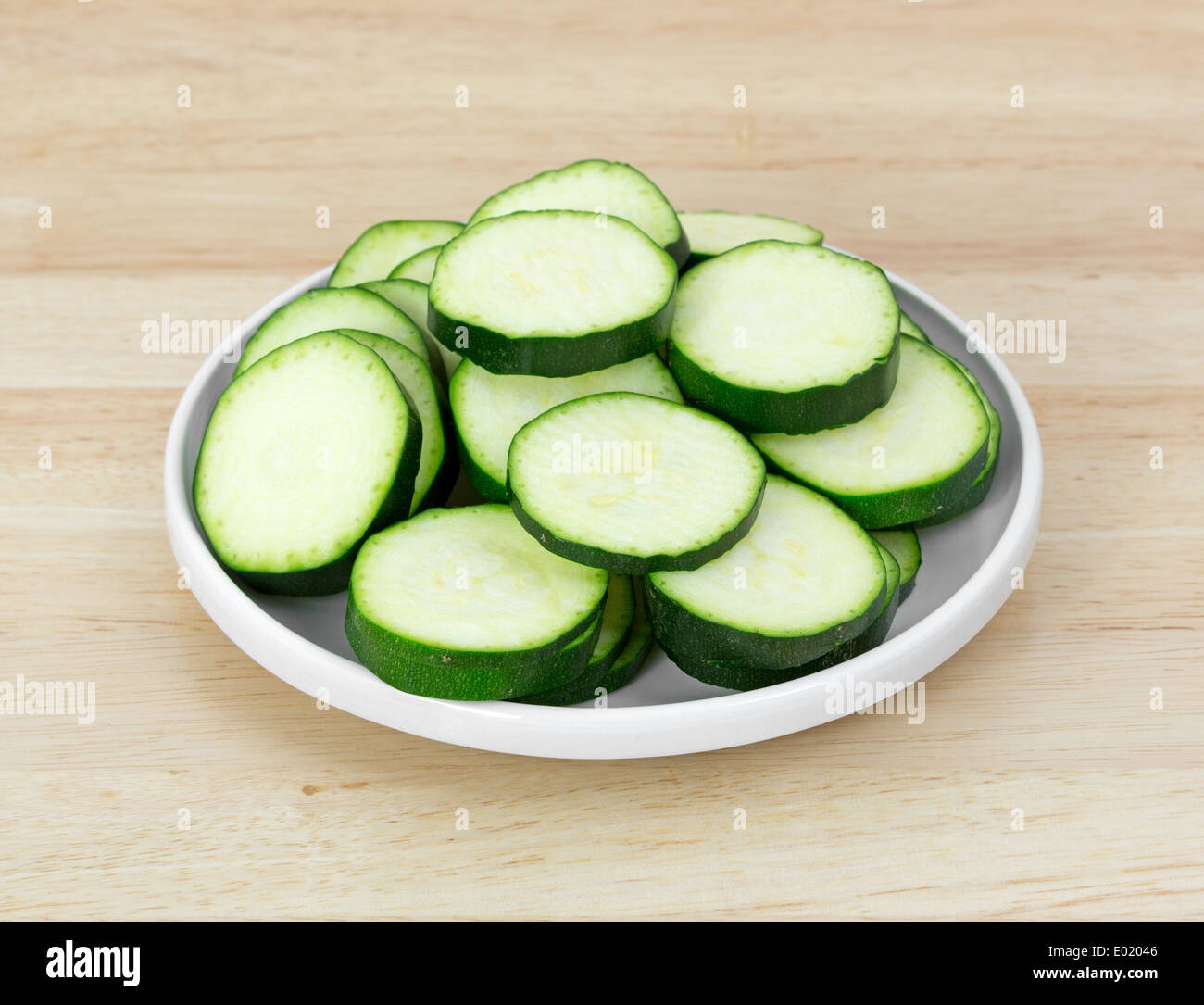 A small dish filled with slices of fresh summer squash on a wood ...