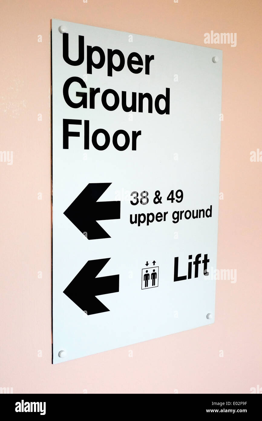 White sign attached to a pink wall giving directions to the lift and ...