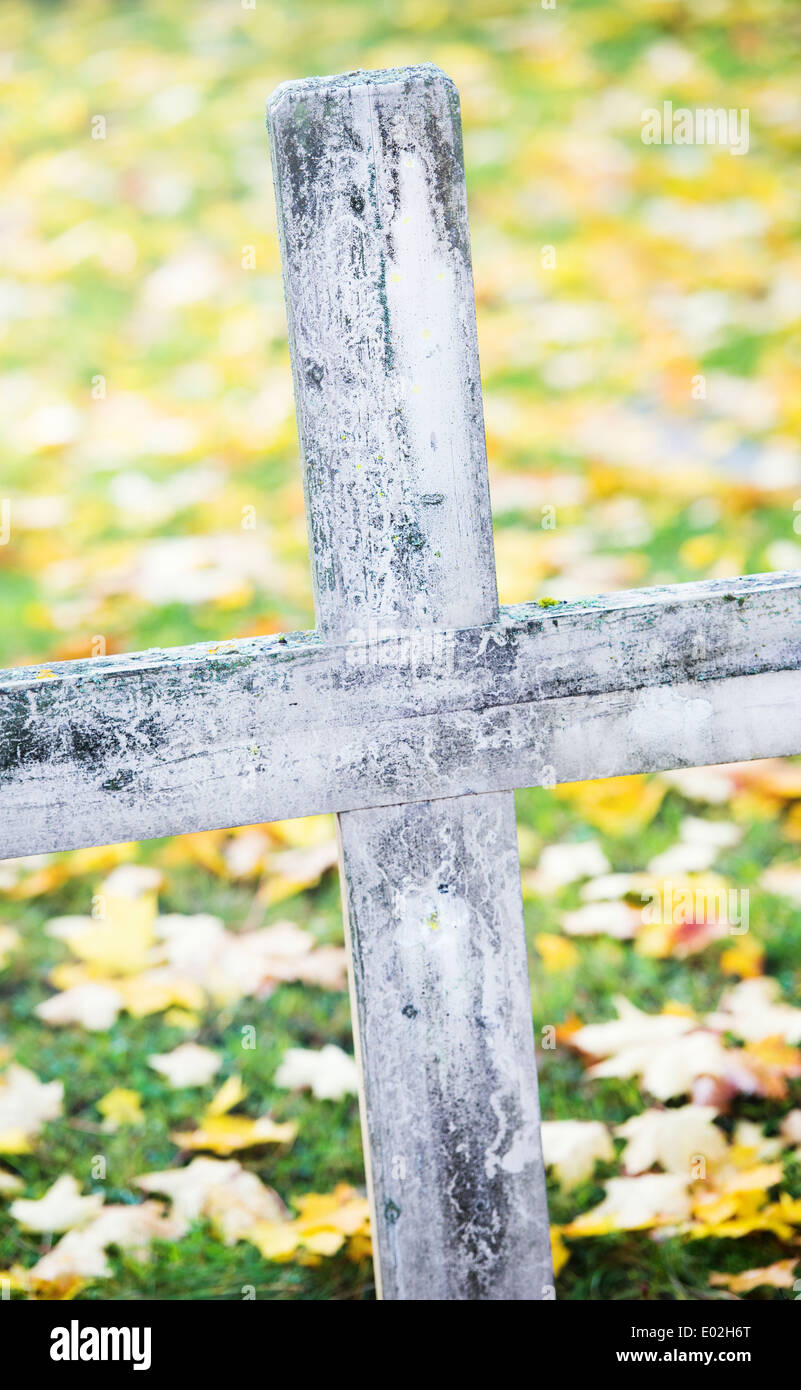 Close up of cross in cemetery with fall leaves in the background ...
