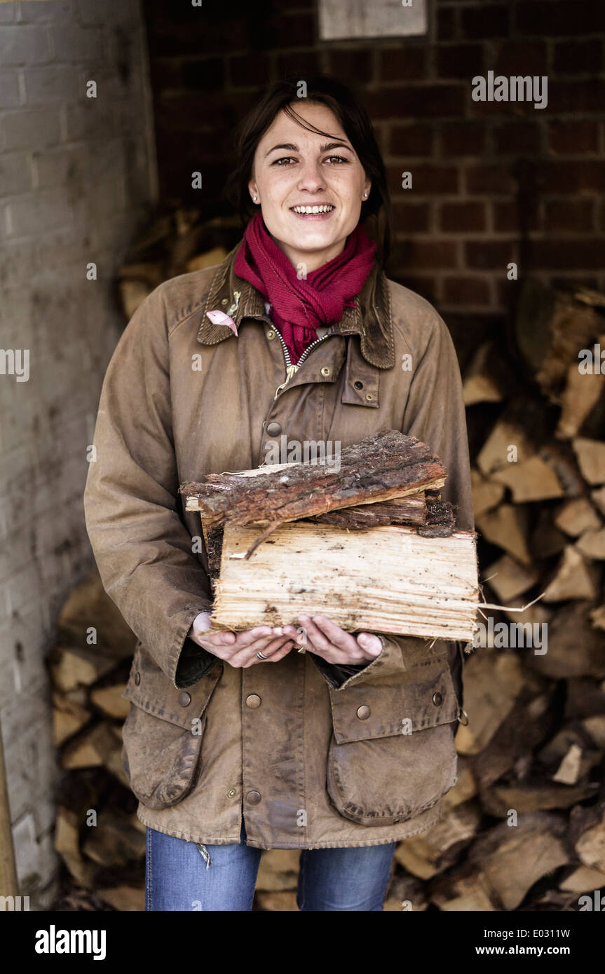 A woman carrying split logs for firewood from a large log store Stock ...