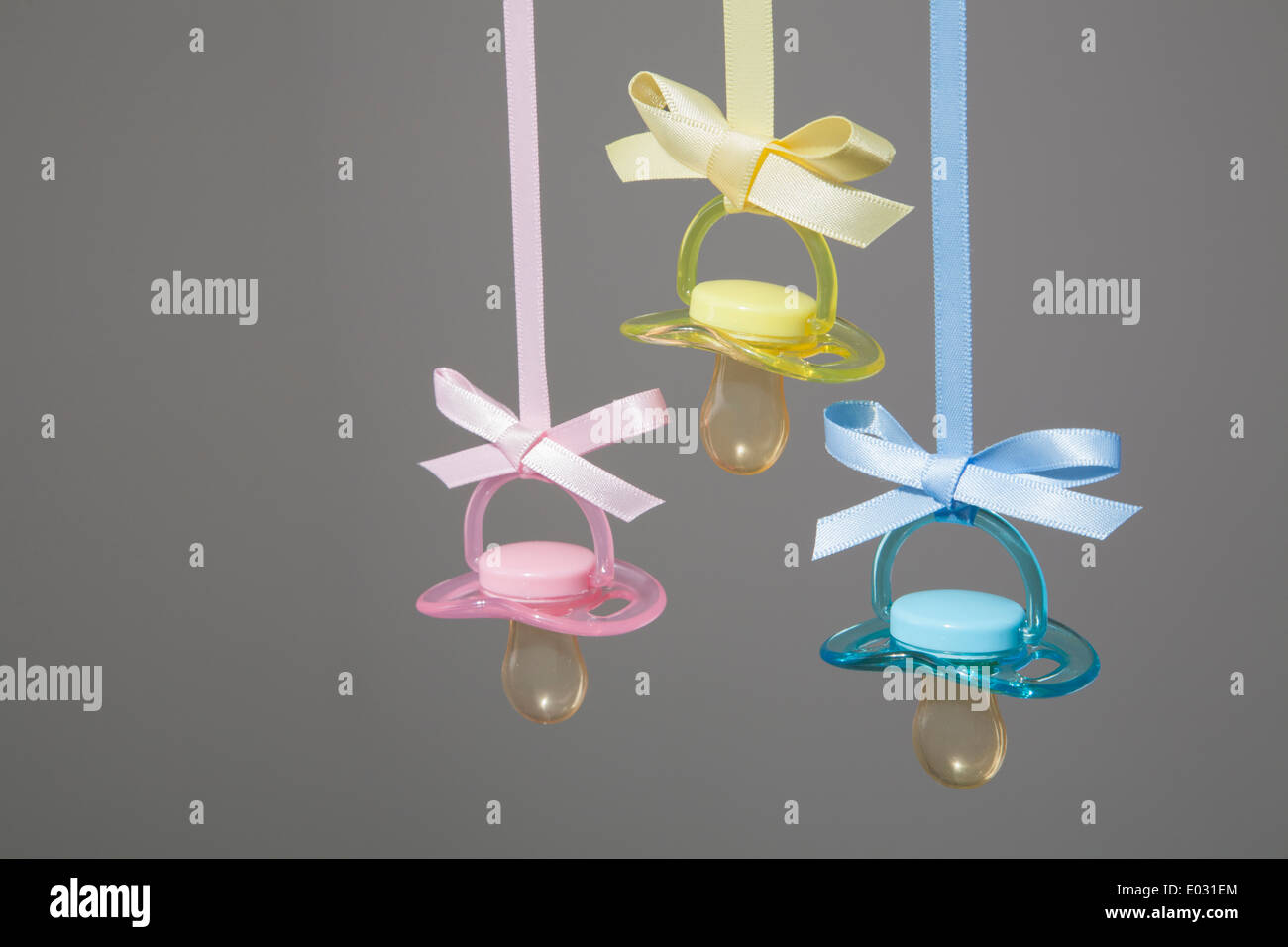 Baby pacifiers hanging from ribbons against a plain background Stock ...