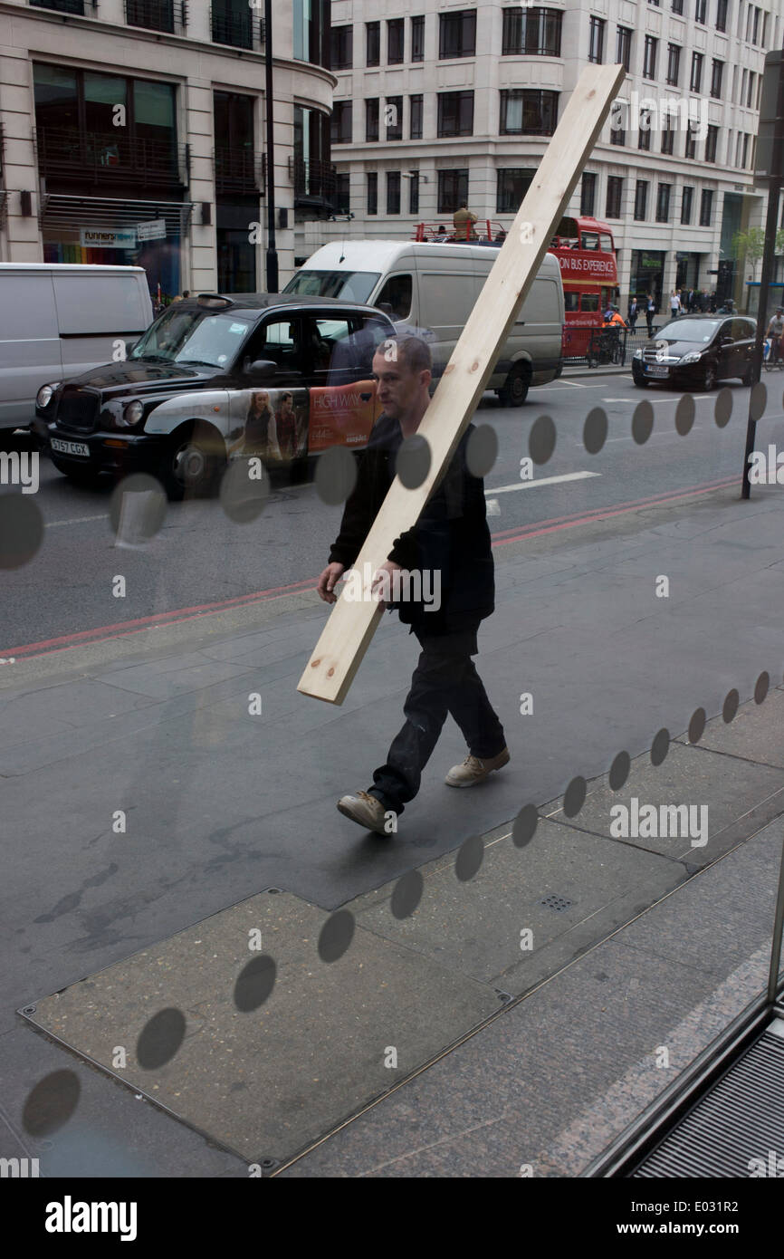 Workman carrying long plank of wood through City of London street Stock ...