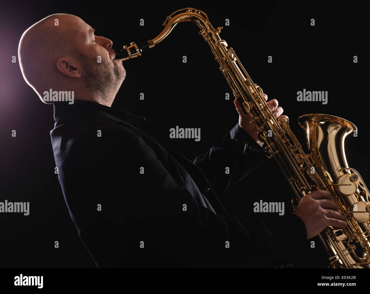Adult musician playing tenor saxophone eyes closed, dark background ...