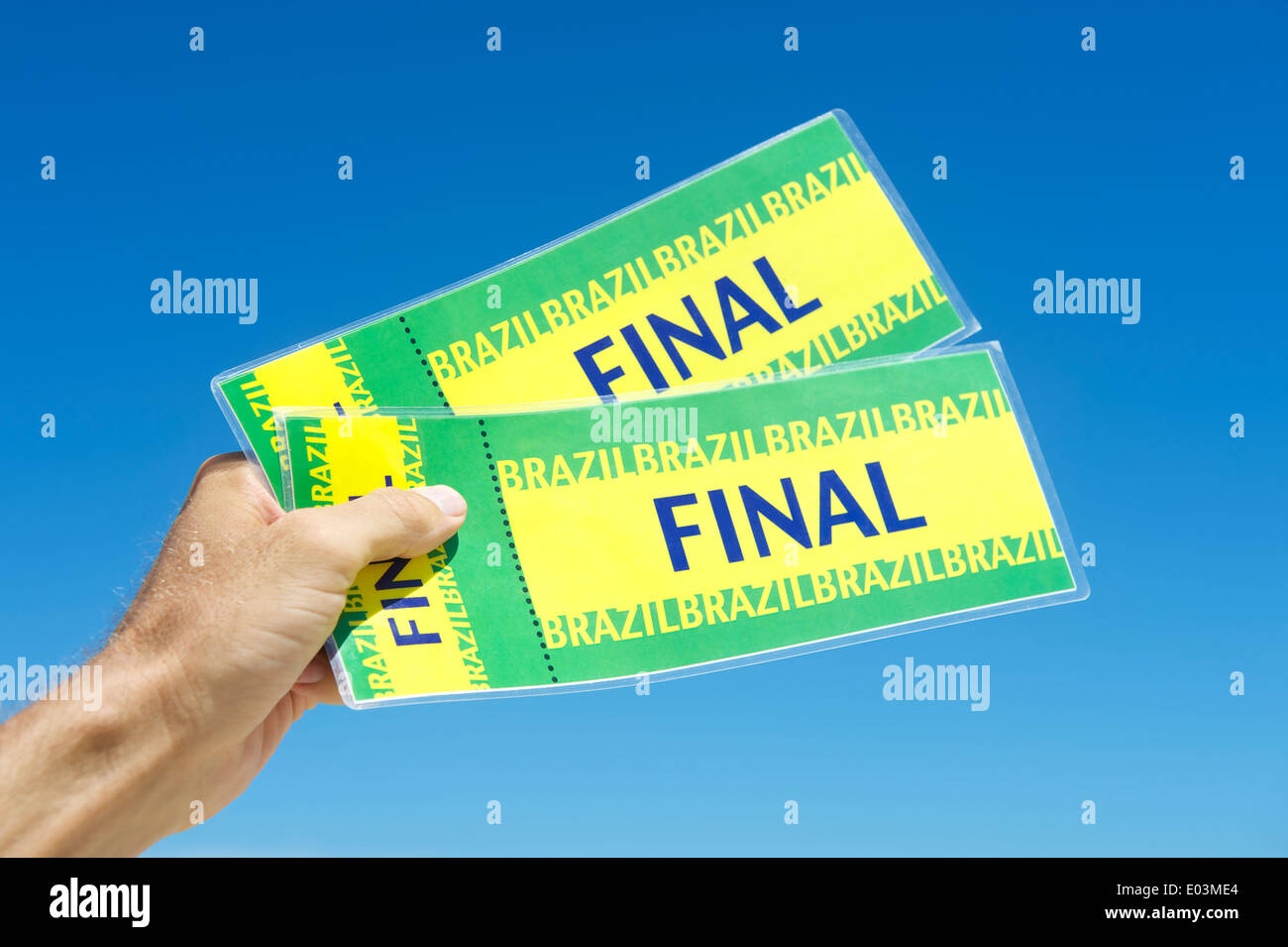 Hand holding two Brazil final tickets against bright tropical blue sky ...