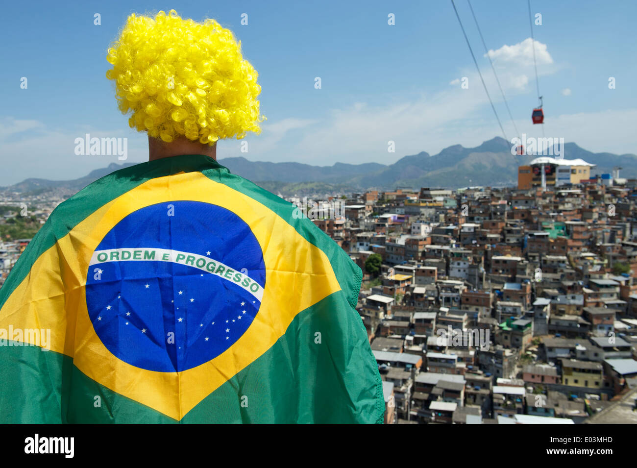 Brazilian football fan standing in Brazil flag in front of favela slum ...
