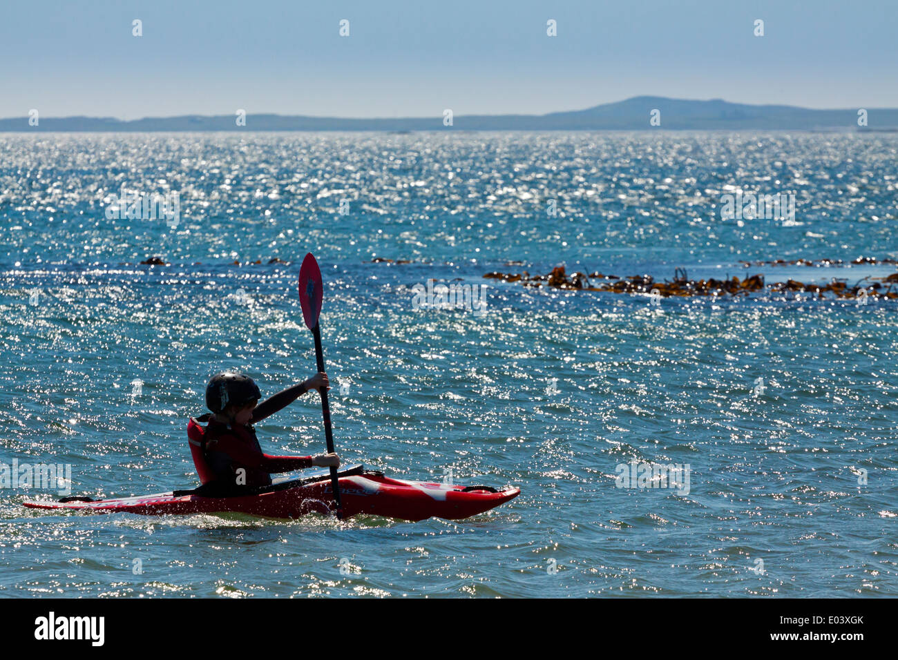 Red kayak in the sea with land in the distance and hills visible on the ...