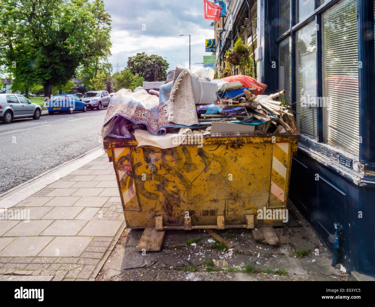 Skip container with building rubble and discarded carpet on pavement ...