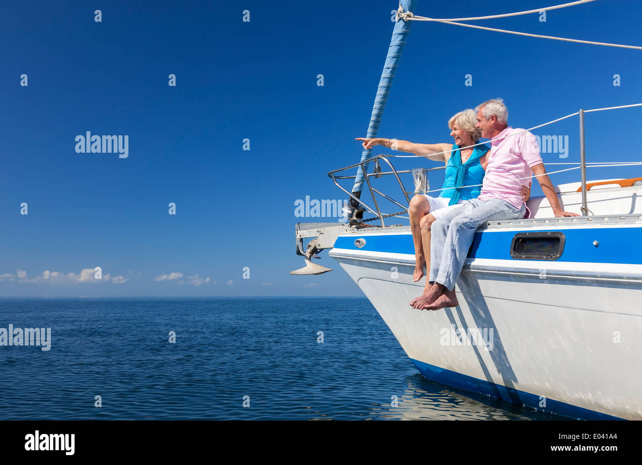 A happy senior couple sitting on the side of a sail boat on a calm blue ...
