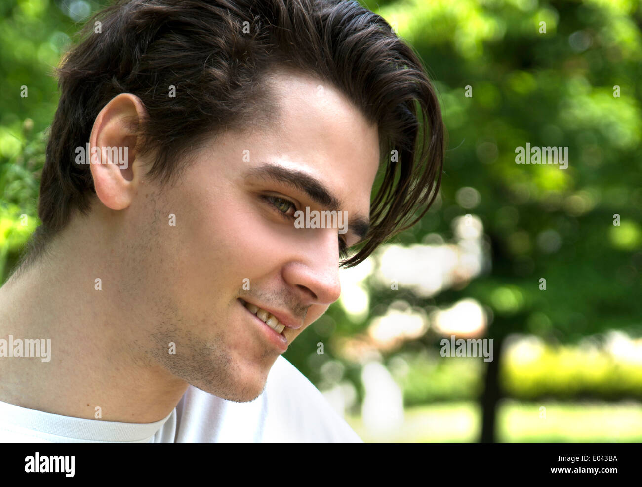 Headshot of attractive young man smiling in nature environment, looking ...