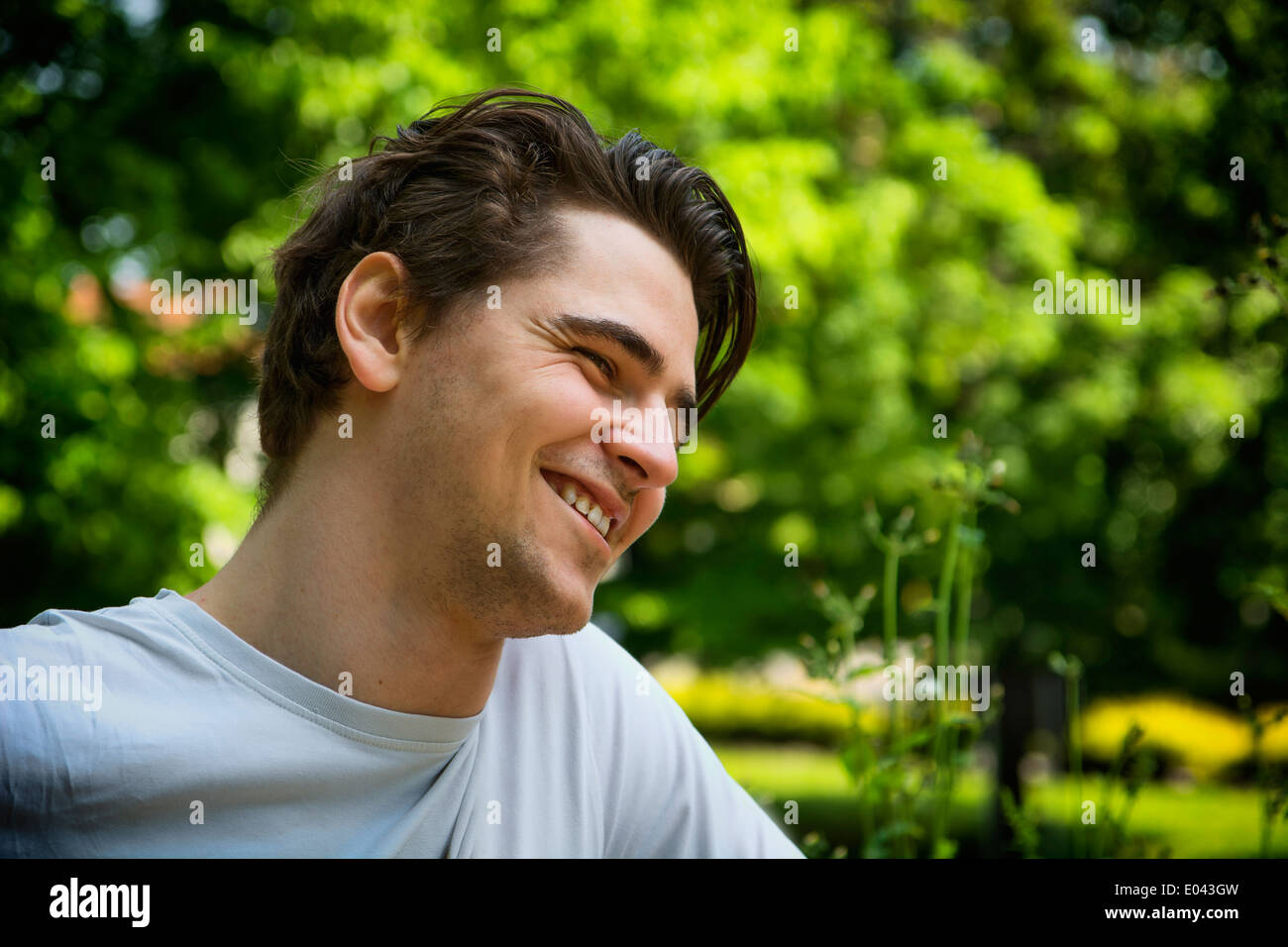 Headshot of attractive young man smiling in nature environment, looking ...