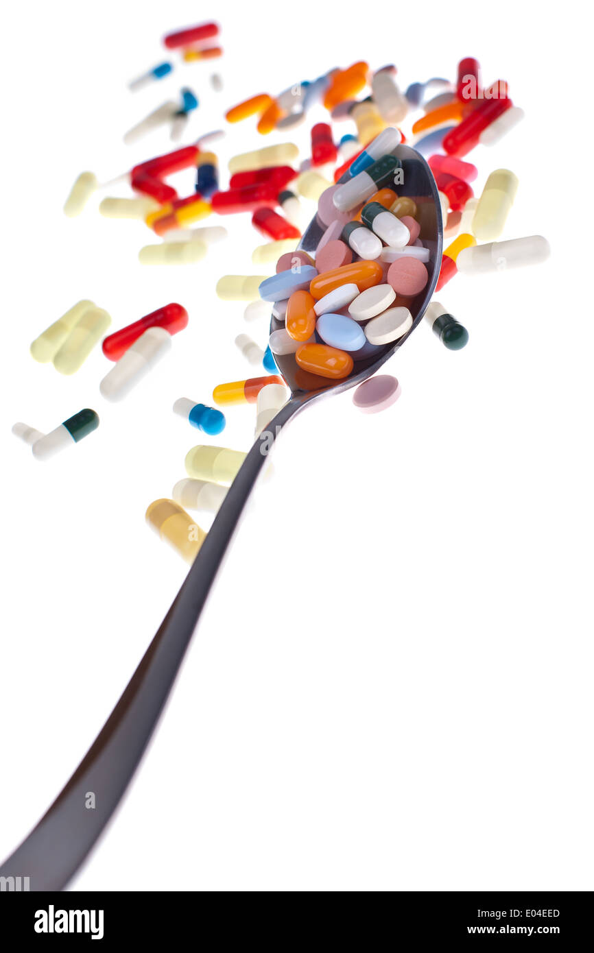 A lot of colored pills and tabs with a spoon over a white background ...