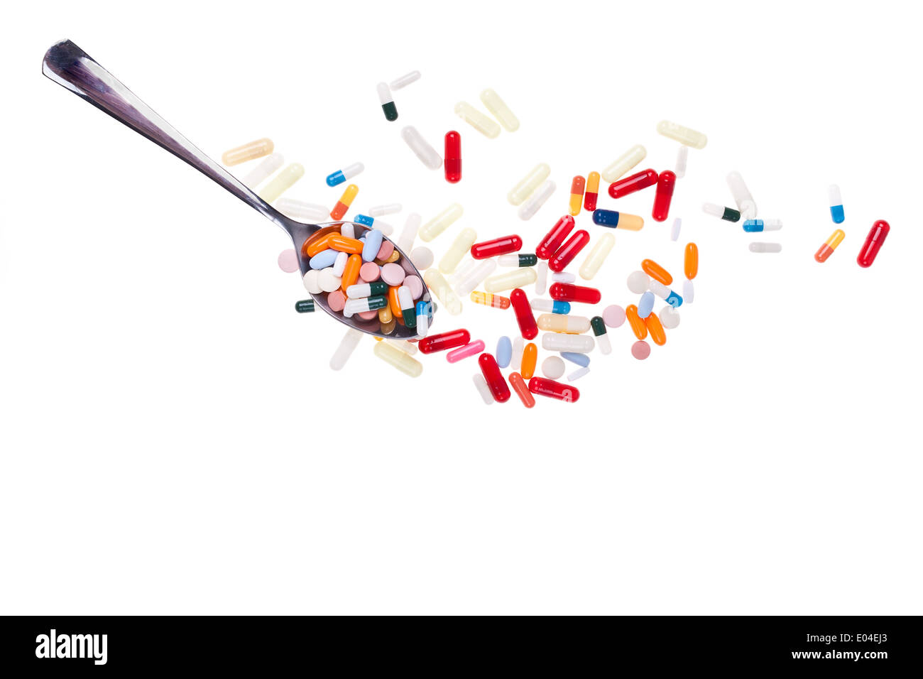 A lot of colored pills and tabs with a spoon over a white background ...