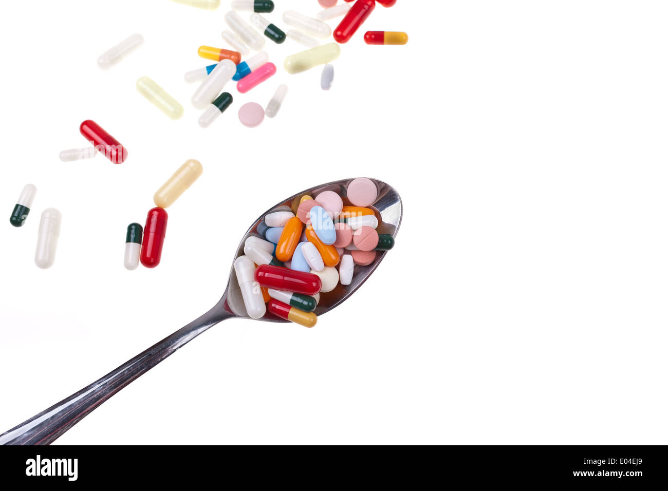 A lot of colored pills and tabs with a spoon over a white background ...