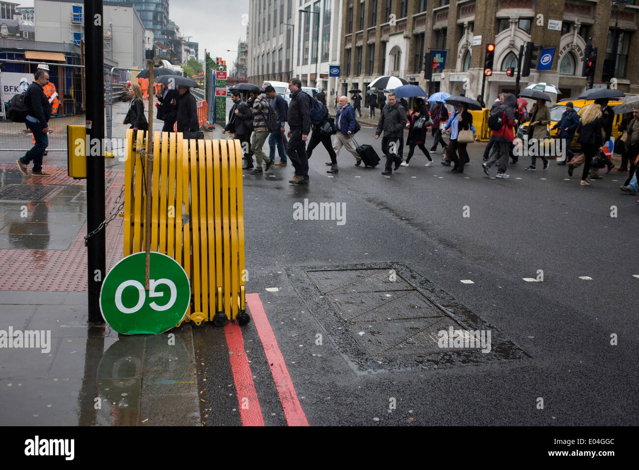 Commuters cross road and upside down GO construction traffic sign in a ...