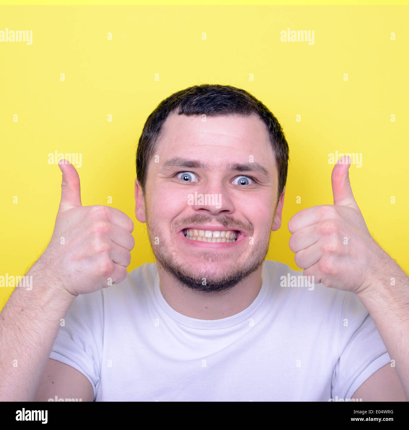 Portrait of with funny expression holding thumbs up against yellow ...