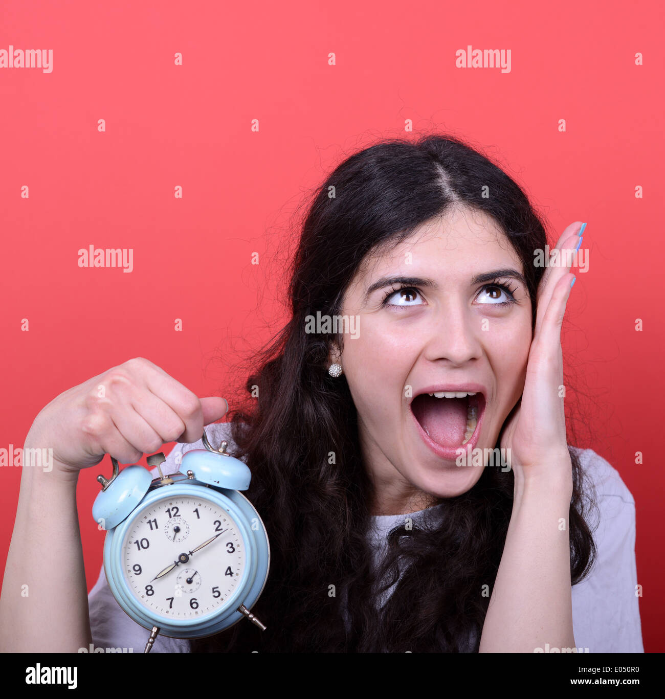 Portrait of girl screaming while holding clock against red background ...