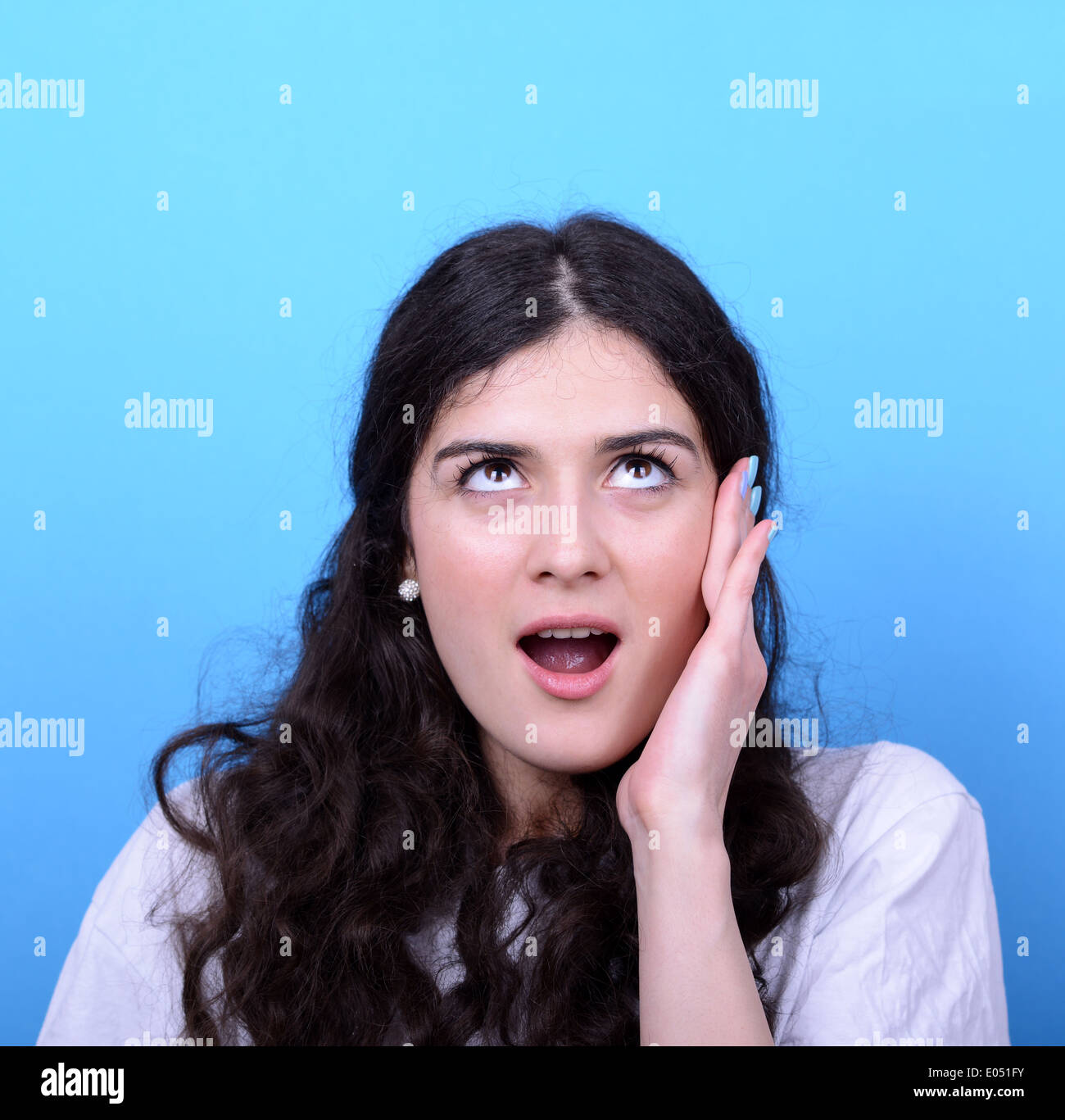 Portrait of girl with shock gesture looking up against blue background ...