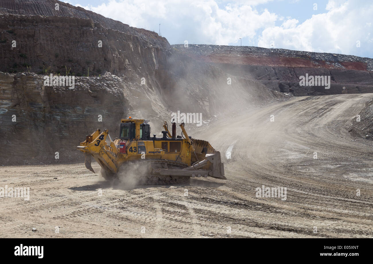 A Komatsu bulldozer trams along in a cloud of dust in a large, open ...