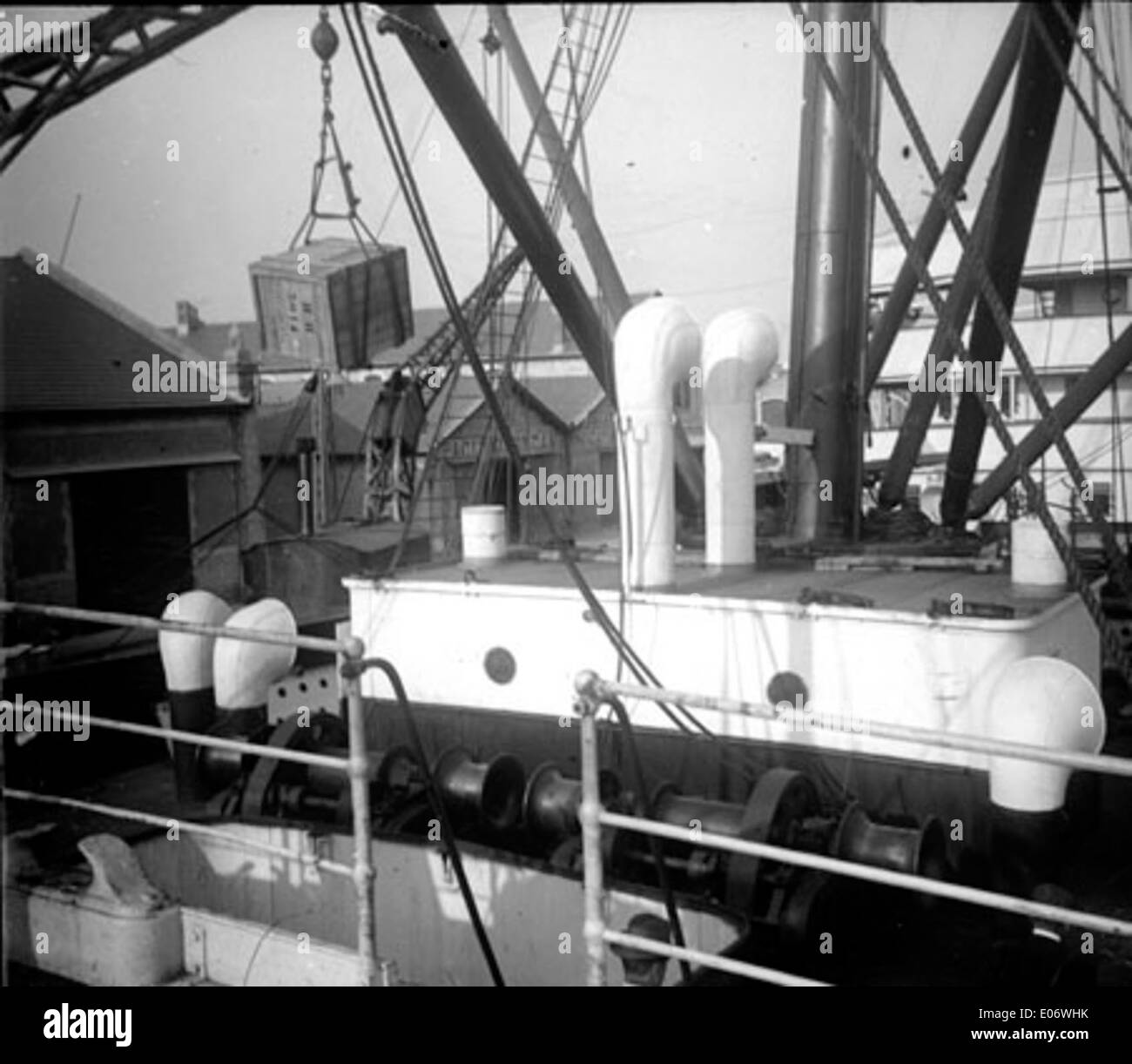The photograph depicts a crate being loaded onto the deck of a boat ...