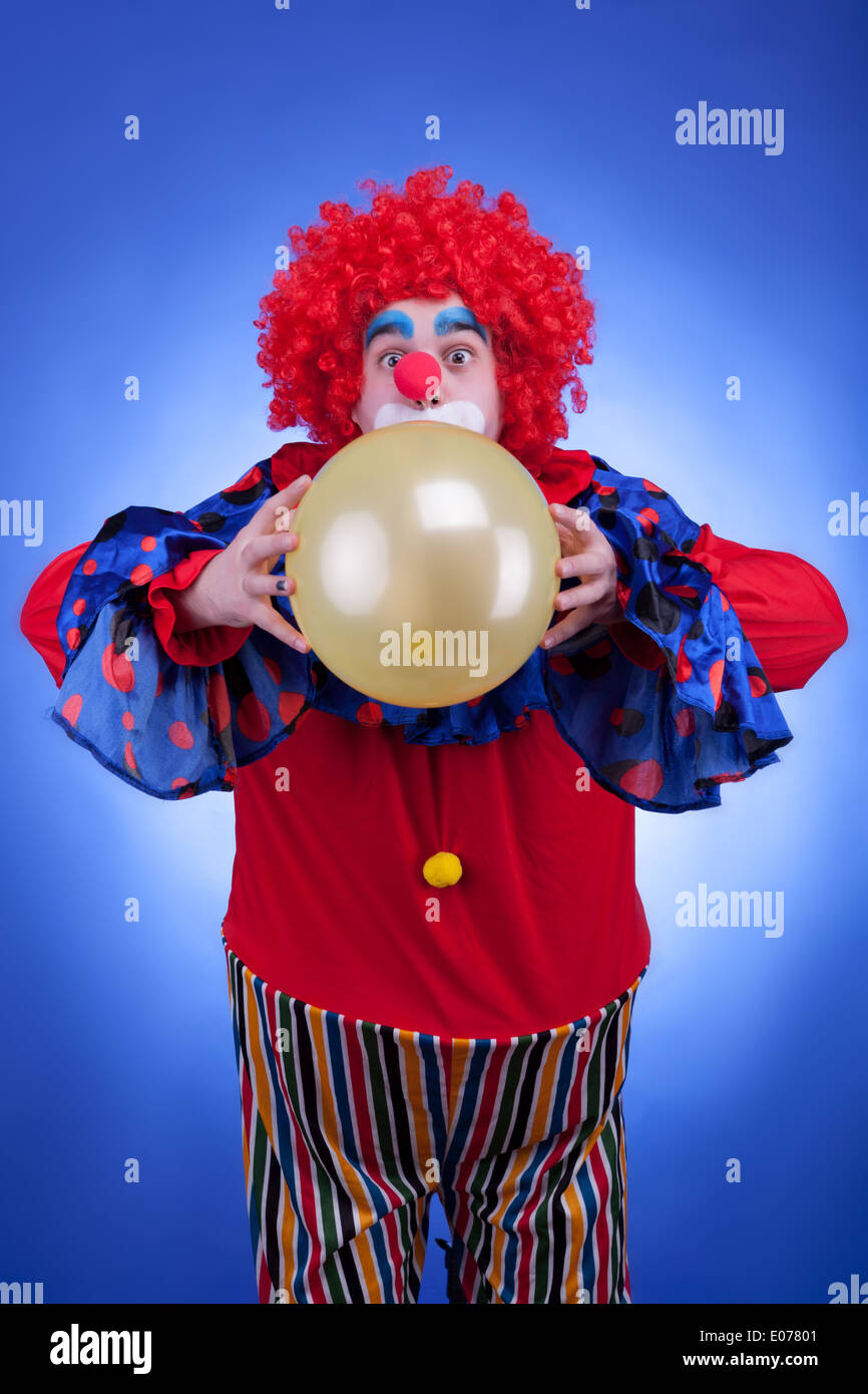 Clown with balloon in red costume on blue background. Studio ...