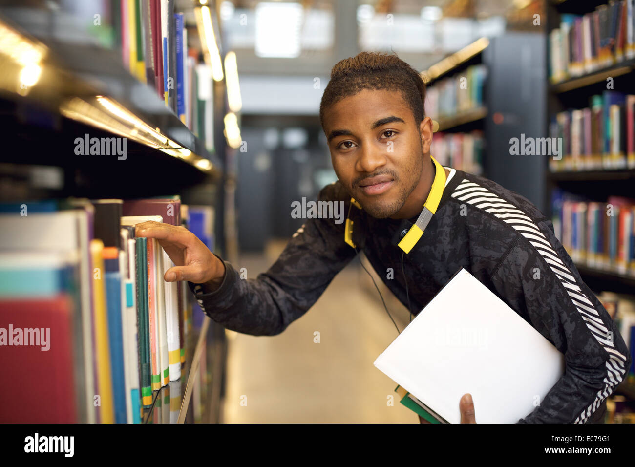 Young Afro-American man getting books from a public library shelf ...