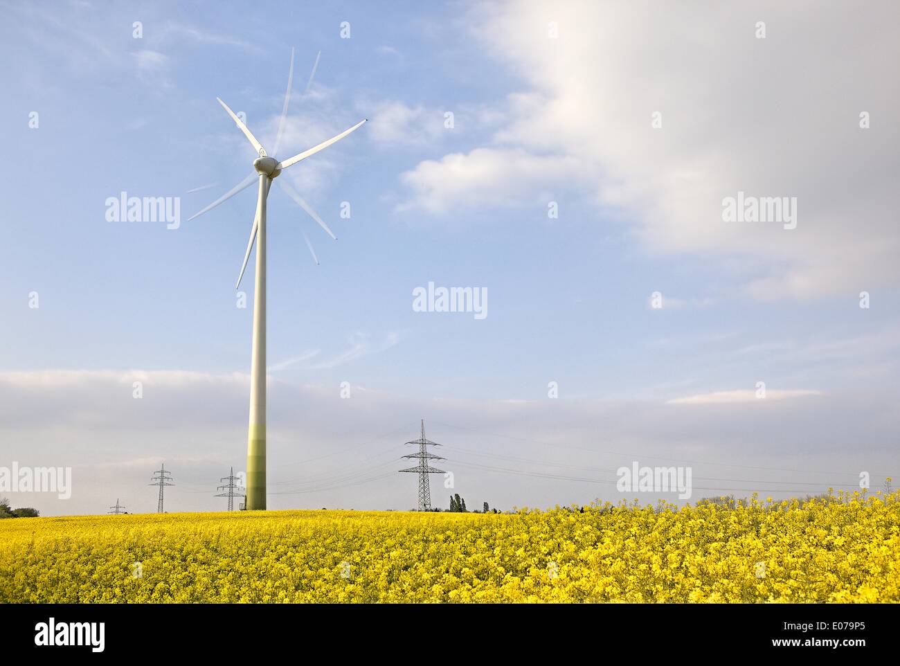 Wind power unit right from a electricity pylon under blue sky trees ...