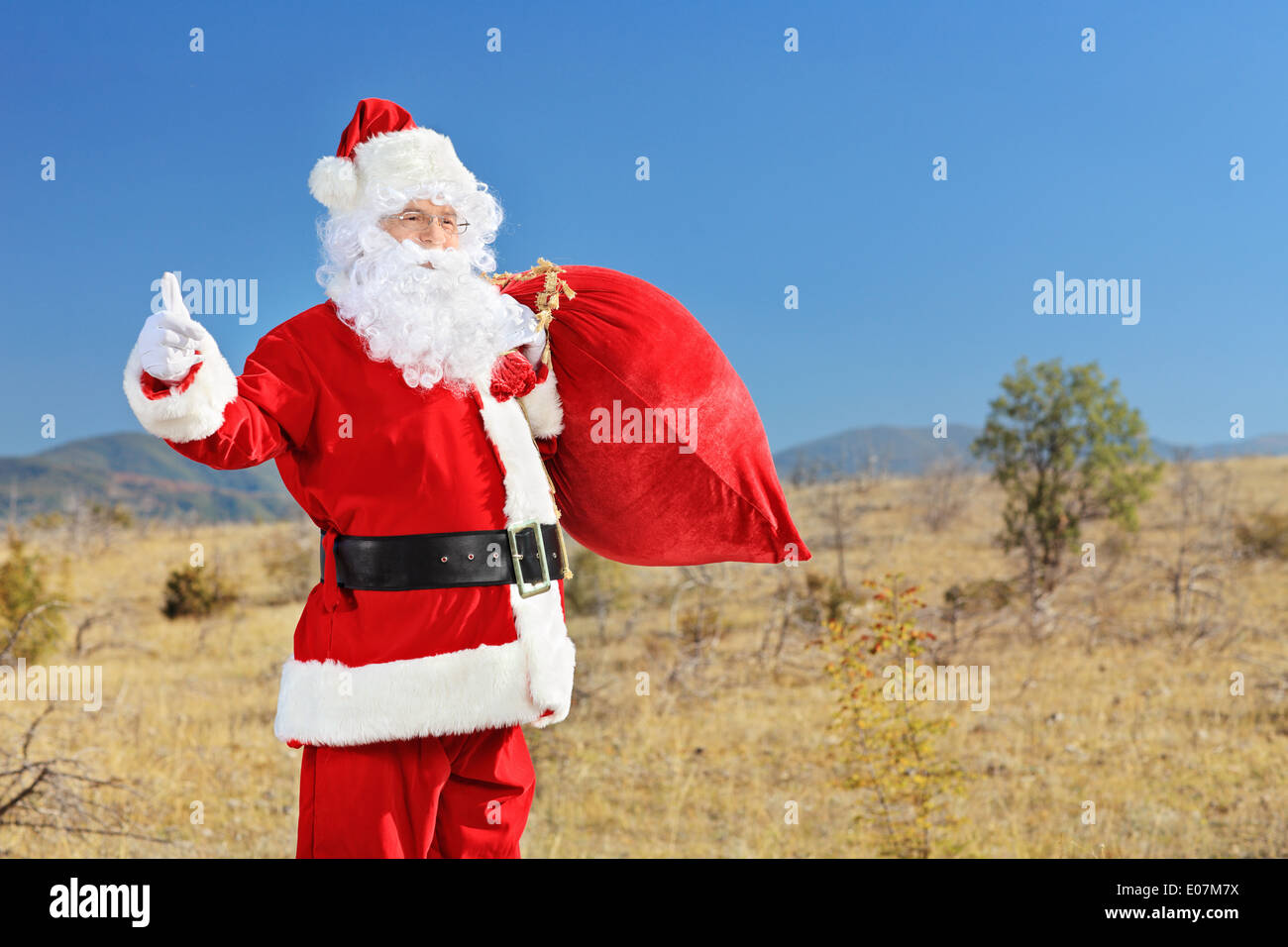 Santa hitchhiking on an open road with his thumb up an holding a bag of ...