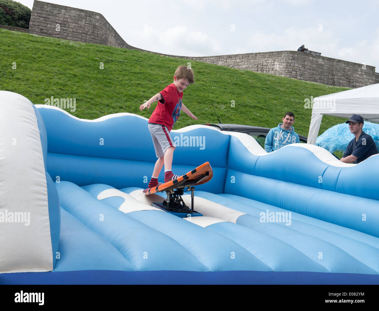 A young boy rides a surf board simulator at a summer fete Stock Photo ...